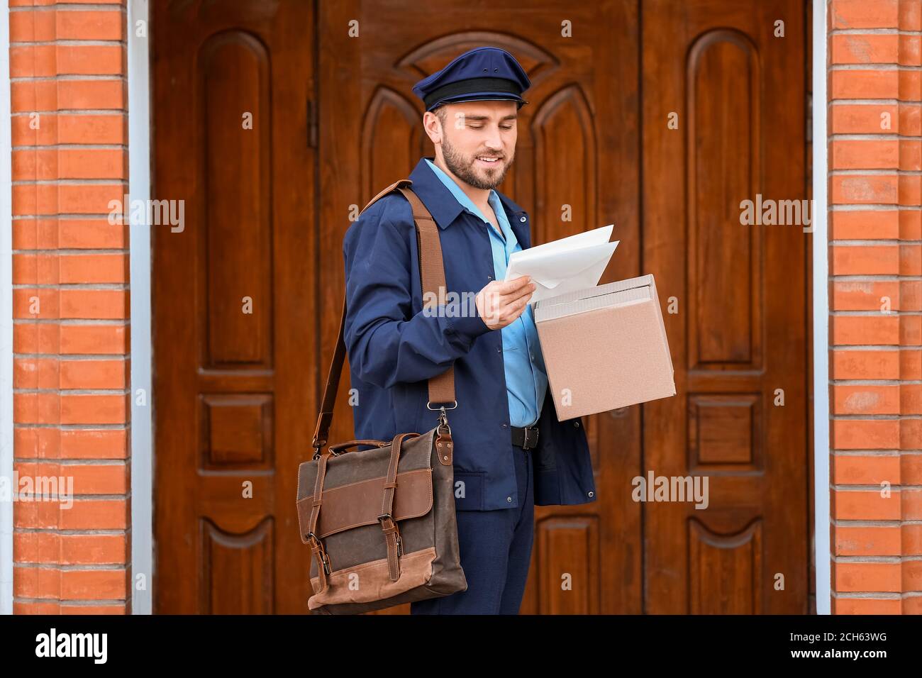 Handsome young postman with parcel and letters outdoors Stock Photo - Alamy