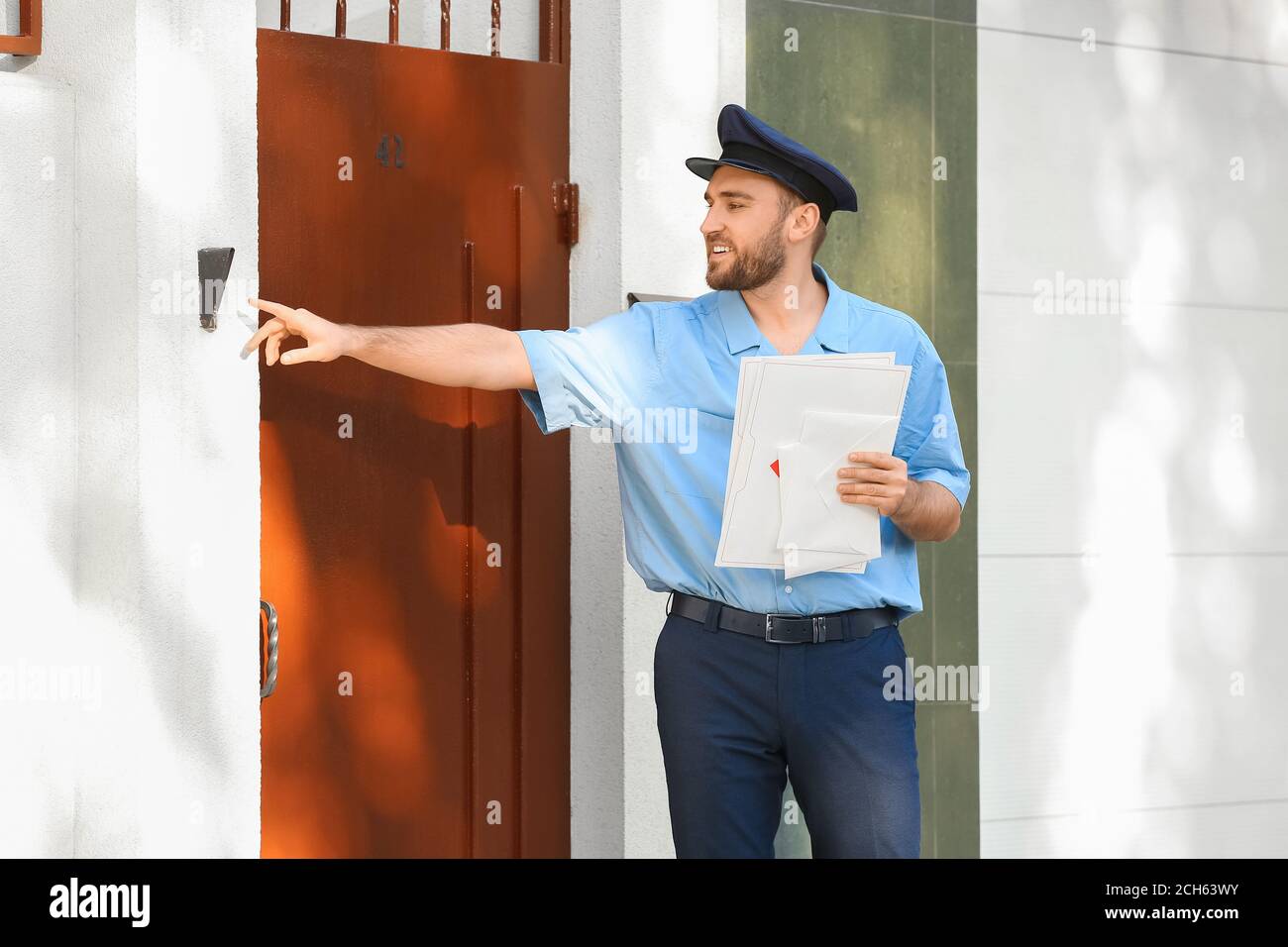 Handsome young postman ringing the door bell outdoors Stock Photo - Alamy
