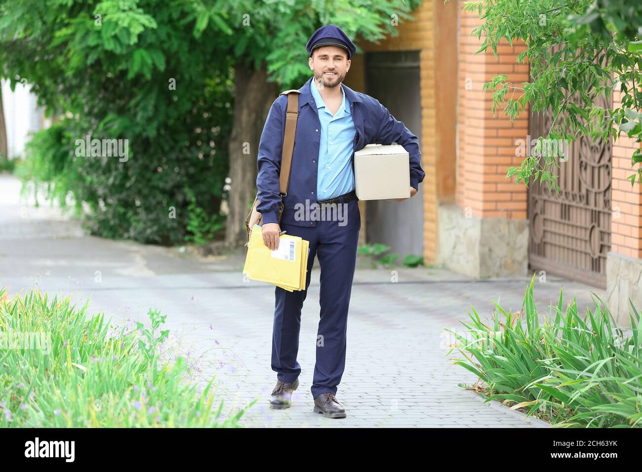 Handsome young postman with parcel outdoors Stock Photo - Alamy