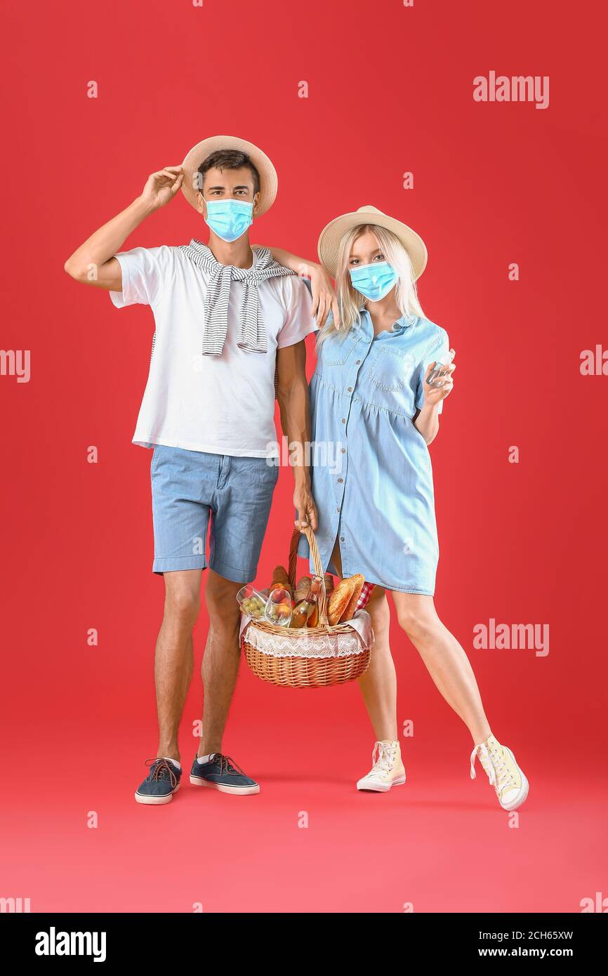 Young couple with protective masks and food for picnic in basket on ...