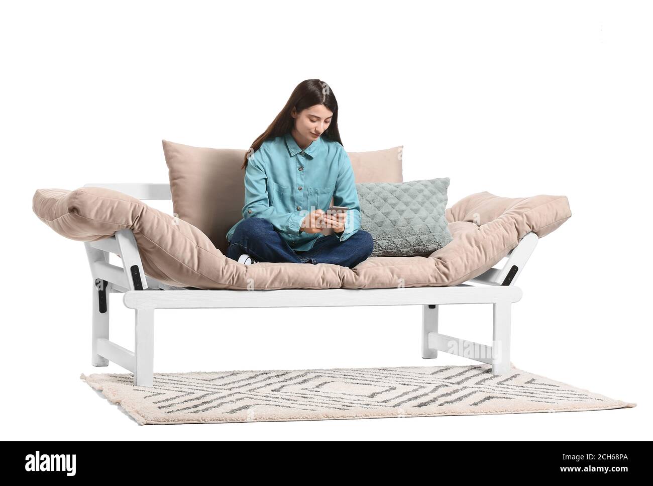 Young woman with mobile phone sitting on sofa against white background ...