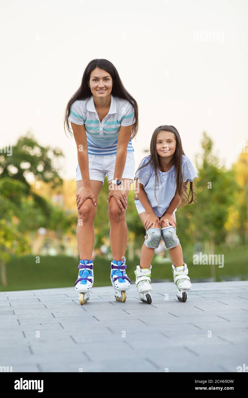 young pretty mother with her little daughter rollerskating in park ...