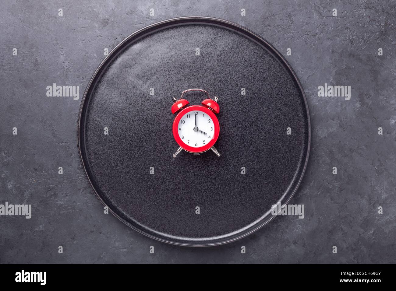 Red alarm clock and empty black ceramic plate on dark stone background ...