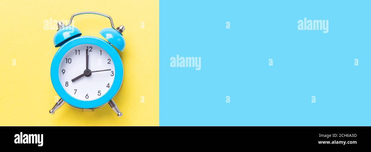Blue alarm clock on two tone color yellow and blue background. Top view ...