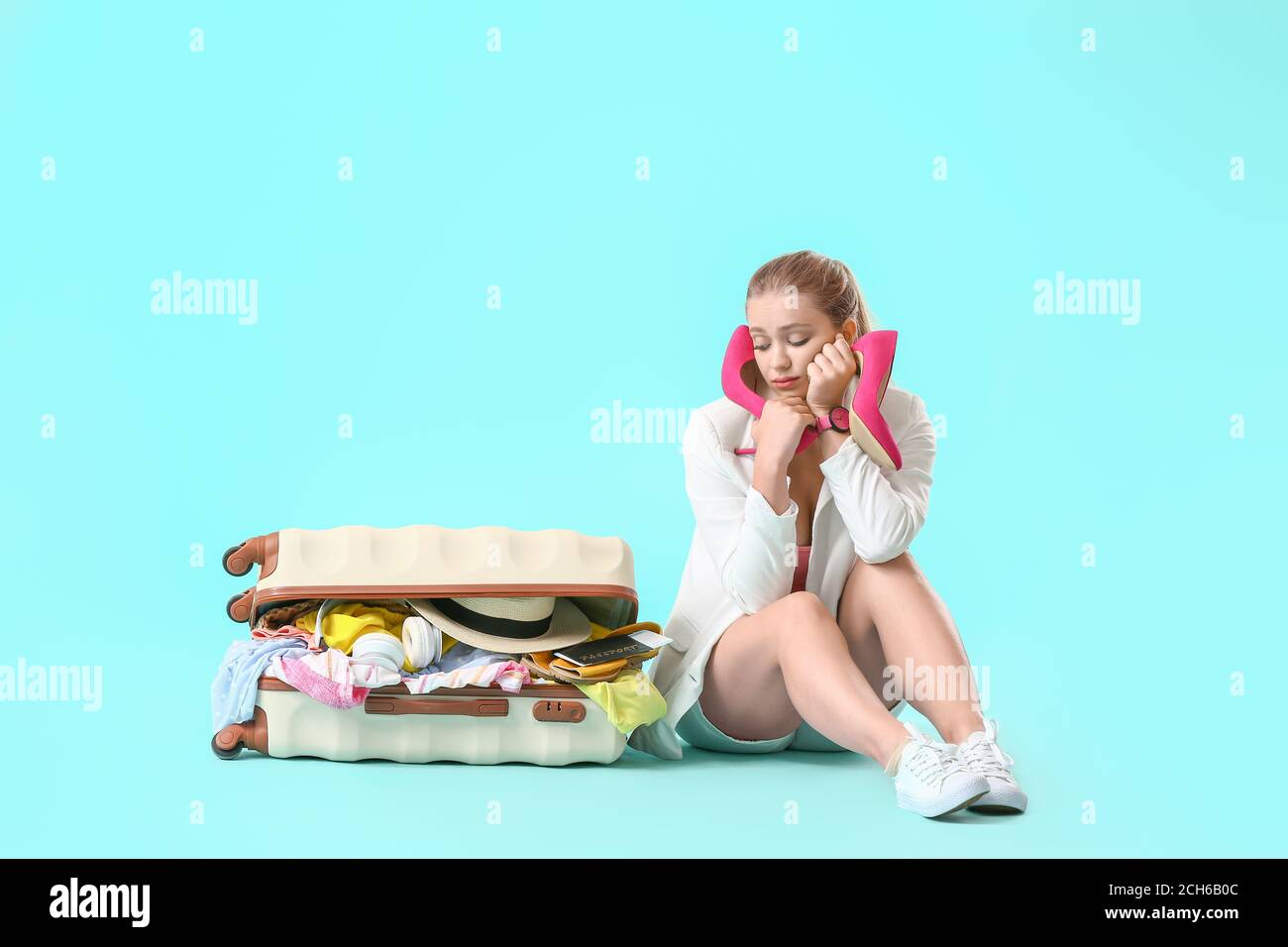 Sad young woman and suitcase with a lot of things on color background ...
