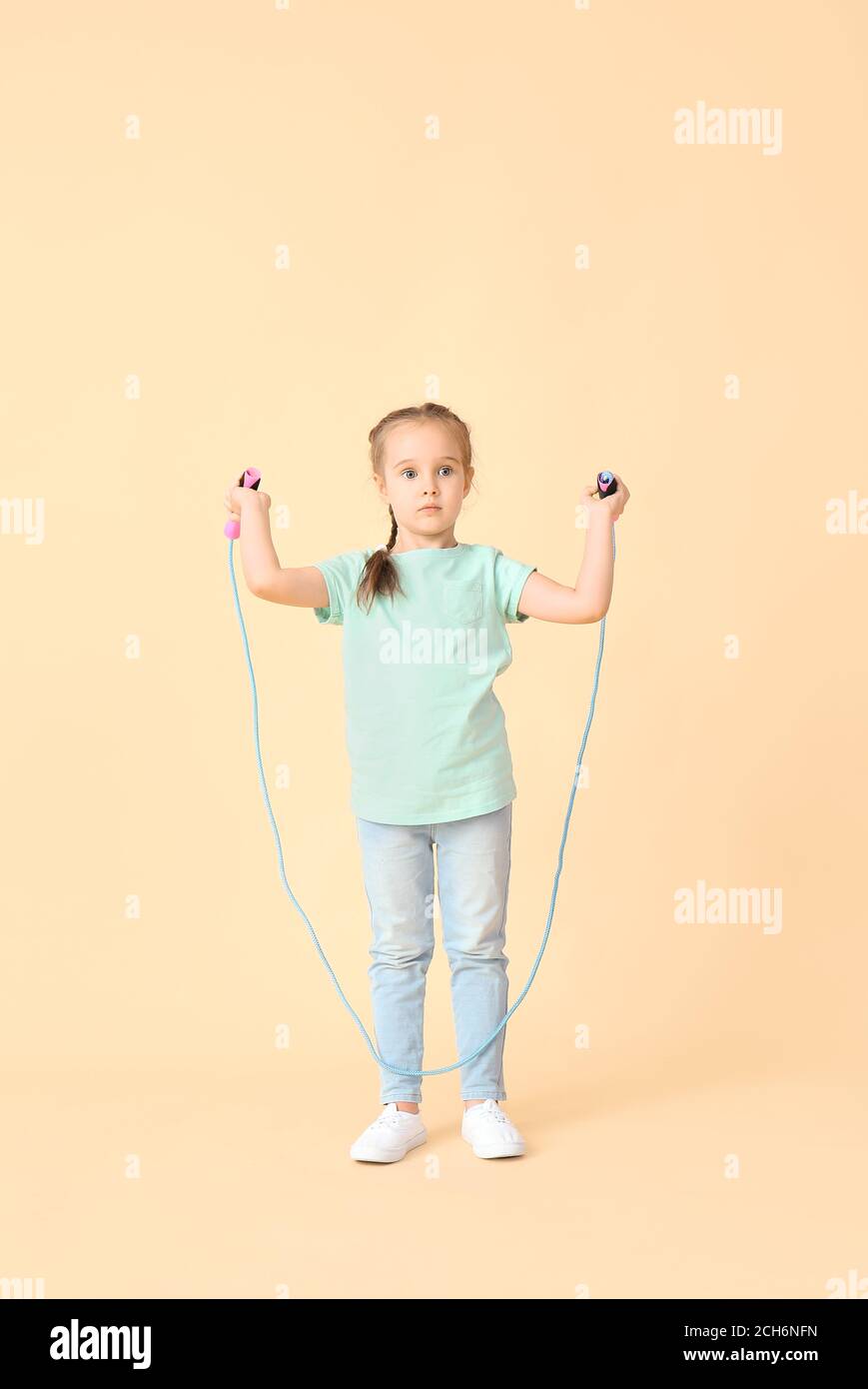 Cute little girl jumping rope against color background Stock Photo - Alamy