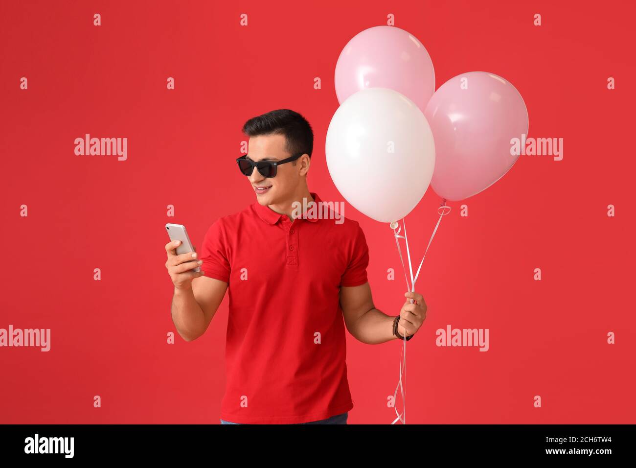 Young man with balloons and mobile phone on color background Stock ...