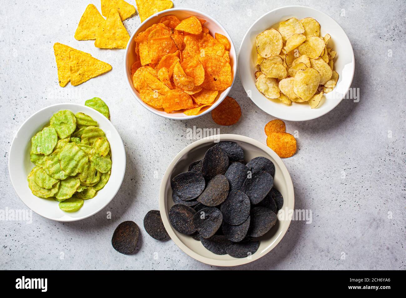 Different types of potato chips in white bowls, gray background. Fast ...