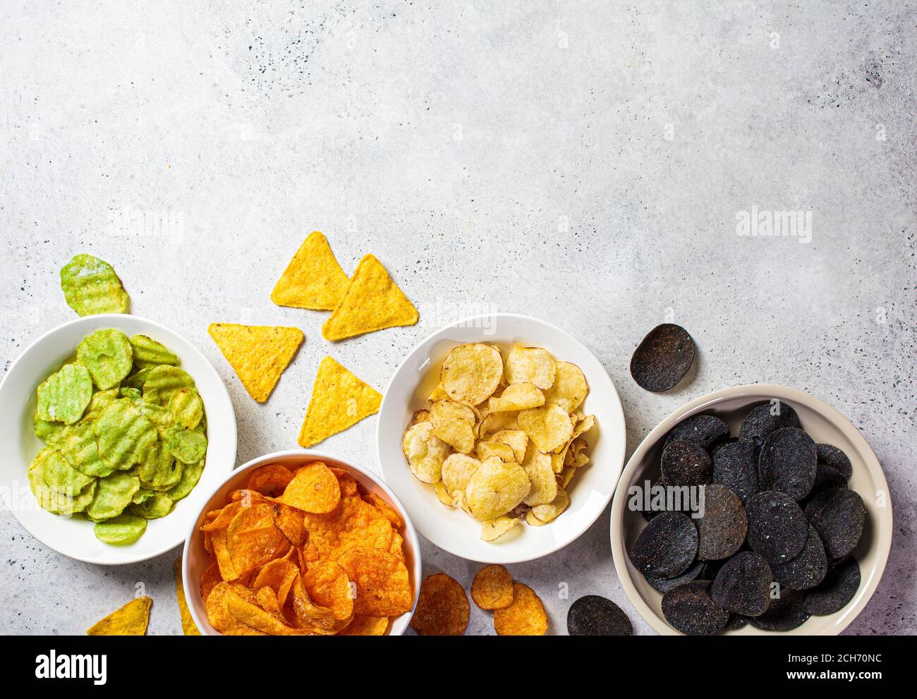 Different types of potato chips in white bowls, gray background. Fast ...