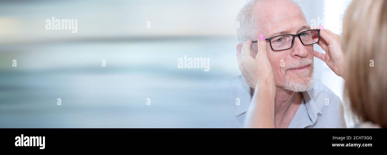 Senior man testing new eyeglasses in optician store; panoramic banner ...