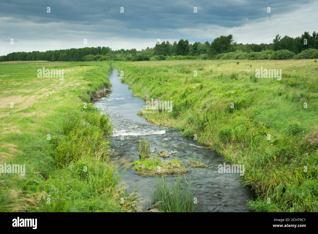 A small river flowing through meadows and clouds in the sky Stock Photo ...