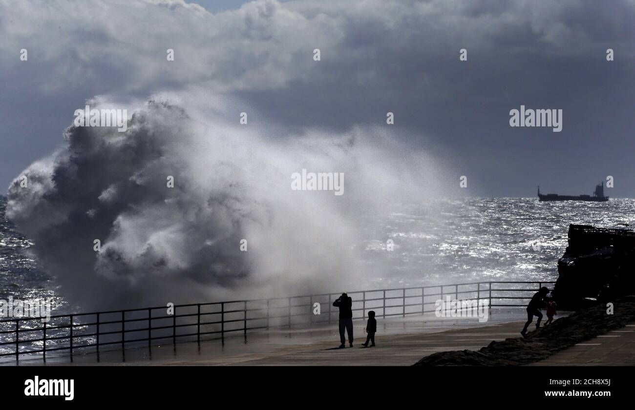 A man takes photographs of huge waves crashing over the seafront in ...