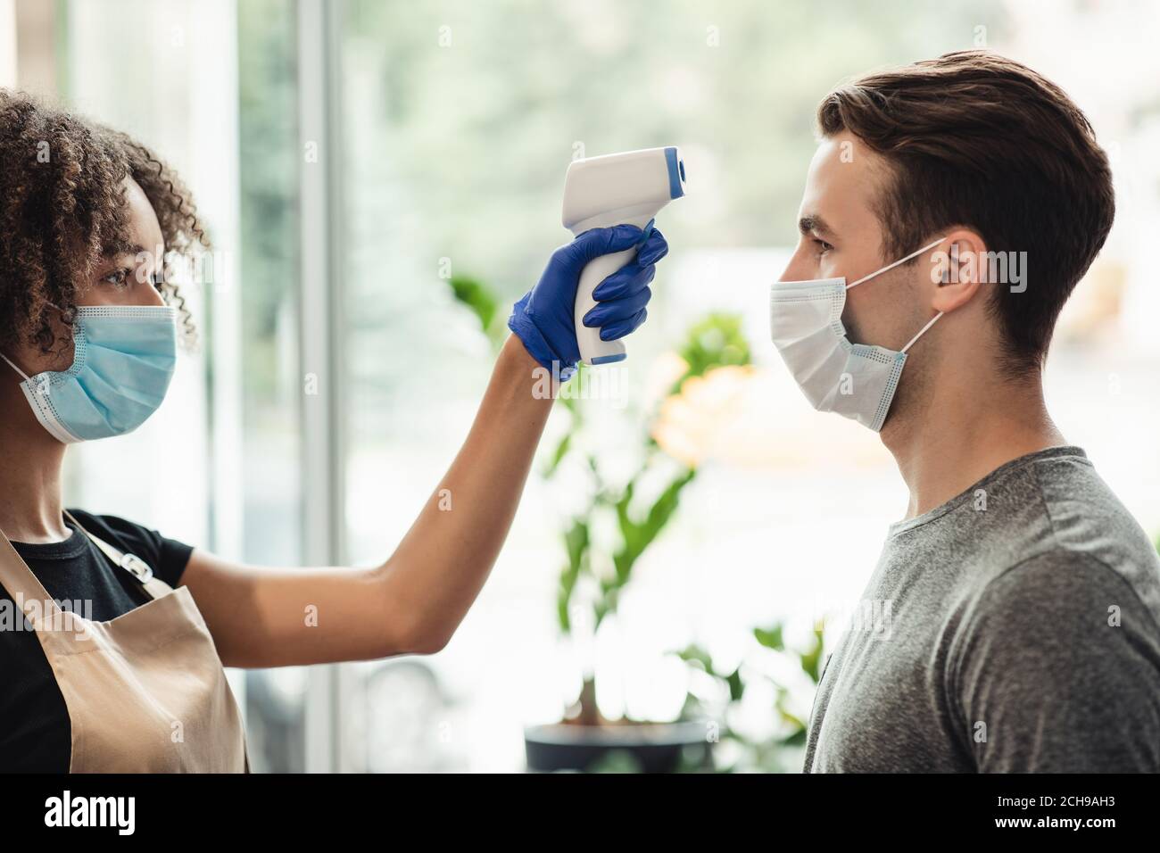 Side view at beauty salon manager measuring body temperature of client ...