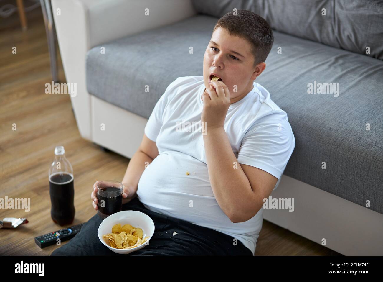 overweight fat boy eat junk food while watching tv alone at home, sit ...