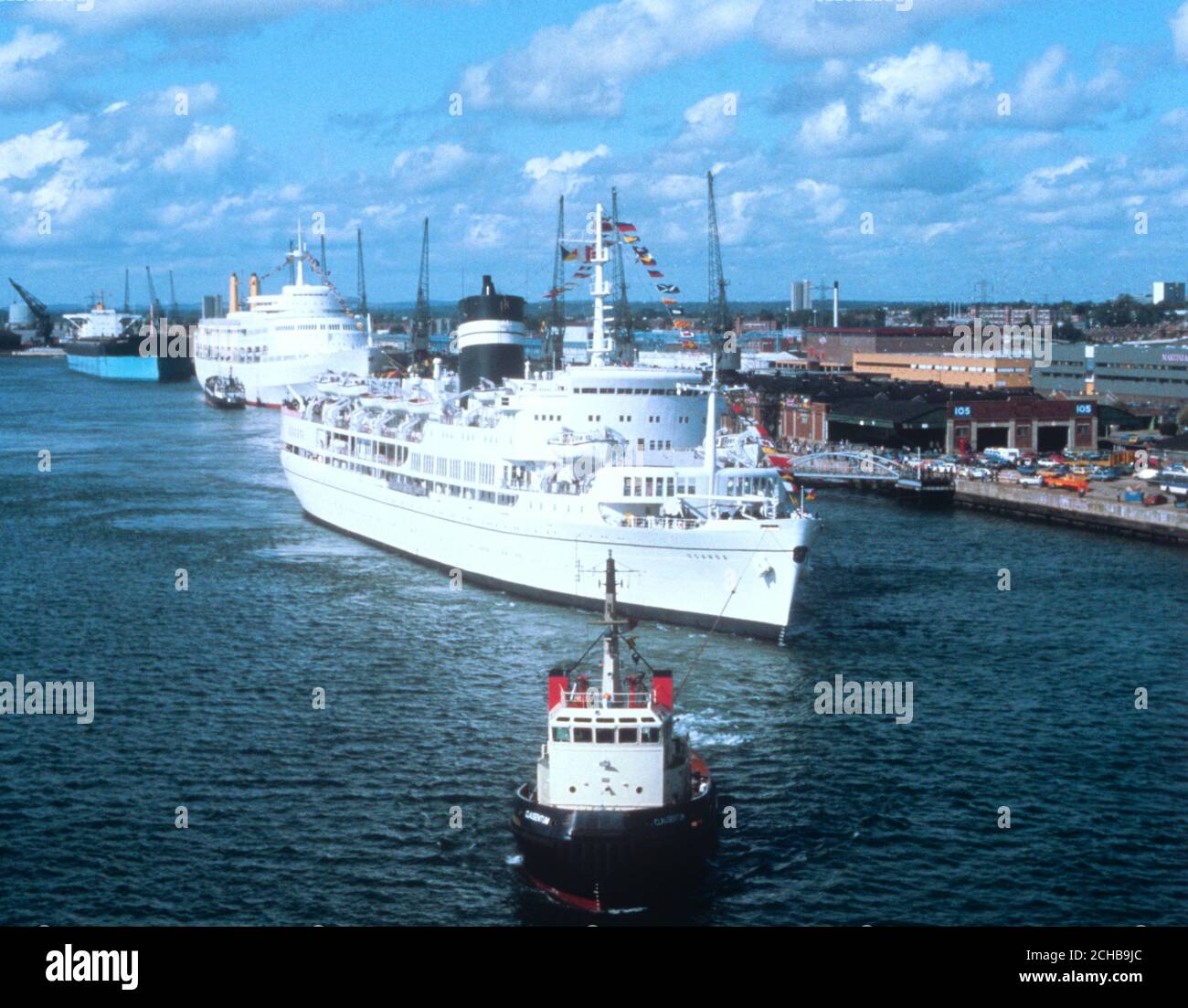 The SS Uganda, festooned with bunting, is tugged away from her quayside ...