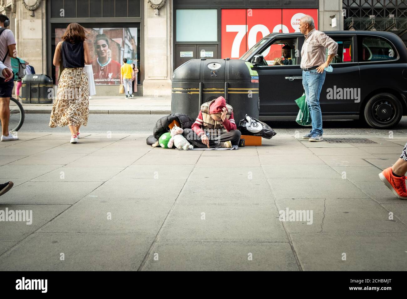 London- September, 2020: A homeless man sits slumped as shoppers walk ...