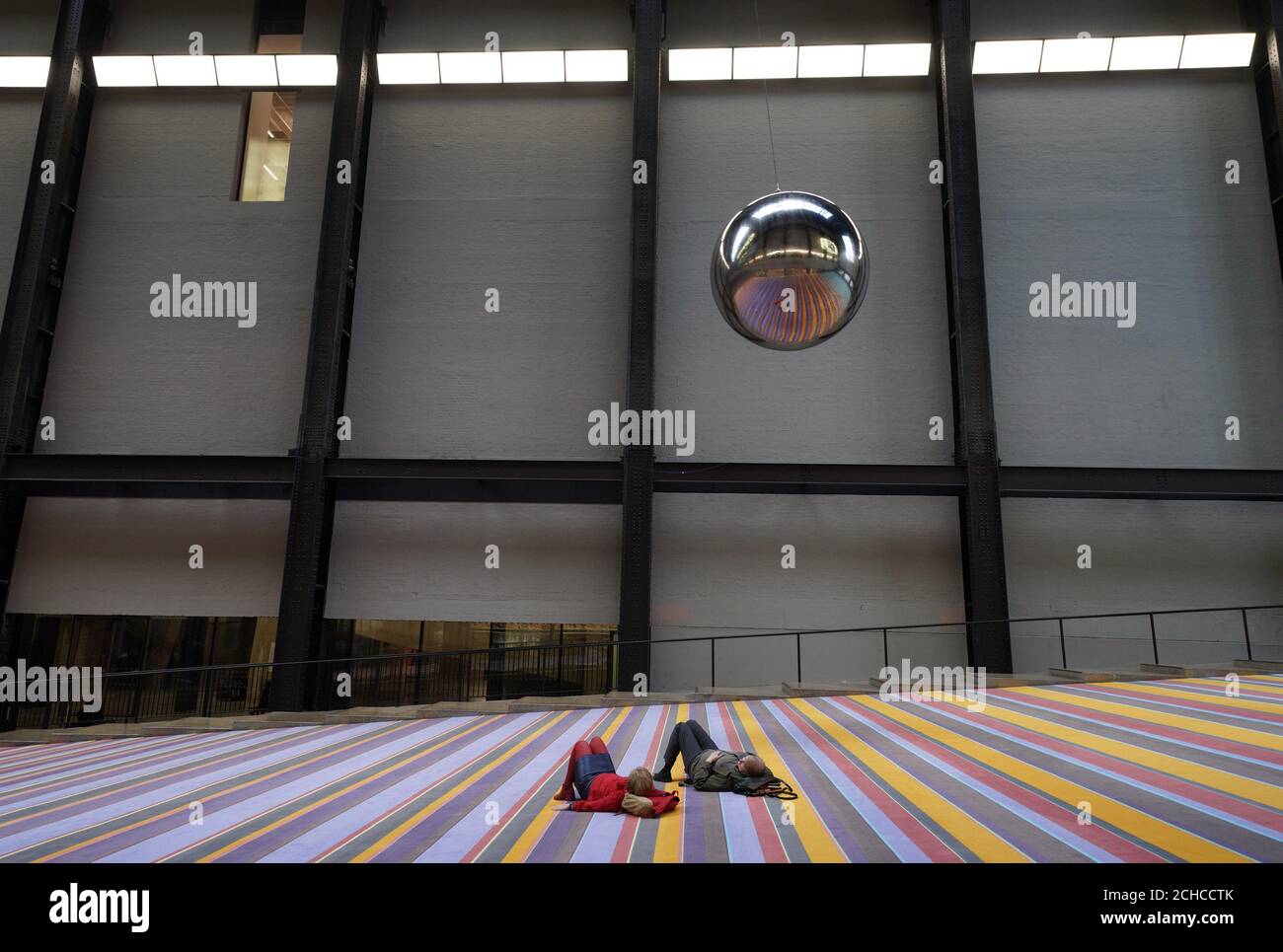 Two women lying underneath a giant swinging pendulum, part of a large-scale interactive ...