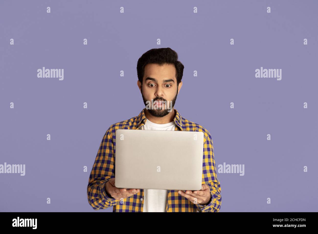 Shocked Indian guy staring at laptop screen with open mouth over lilac ...