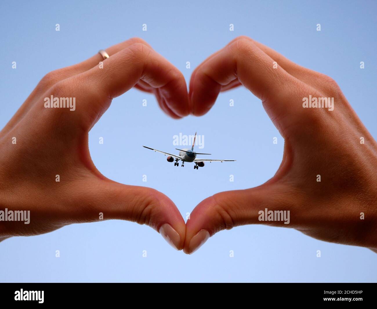 Female hands in shape of love heart and the airplane flying into the ...