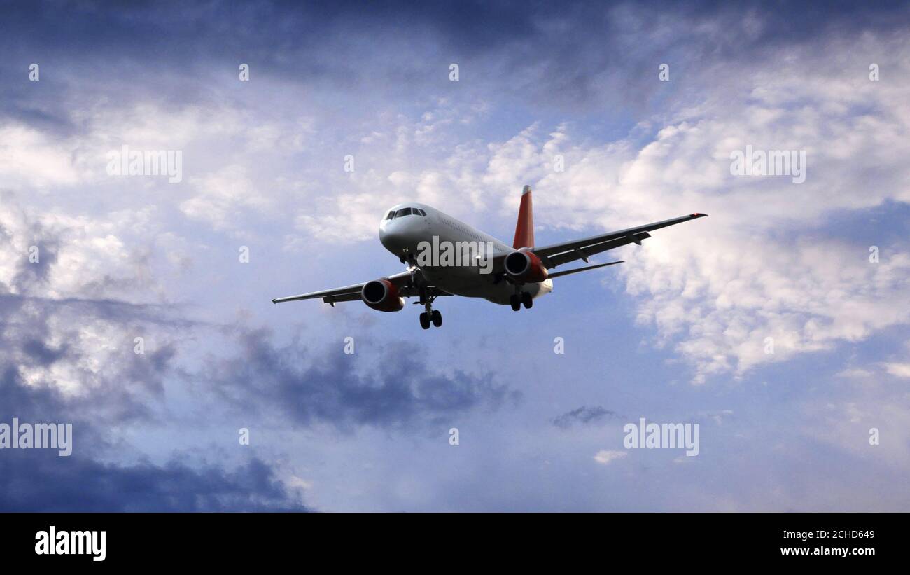 Airplane flying under beautiful evening clouds, front view. Concept of ...
