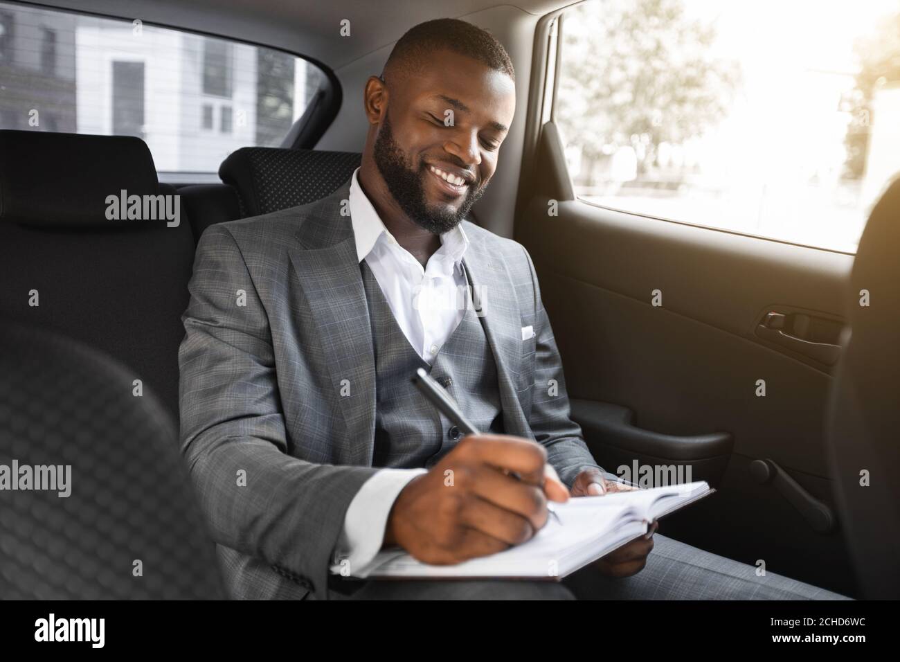 Happy black businessman sitting in car, taking notes Stock Photo - Alamy