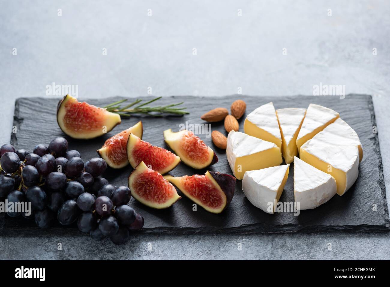 Brie cheese with figs and grapes on black slate. Gourmet cheese platter ...