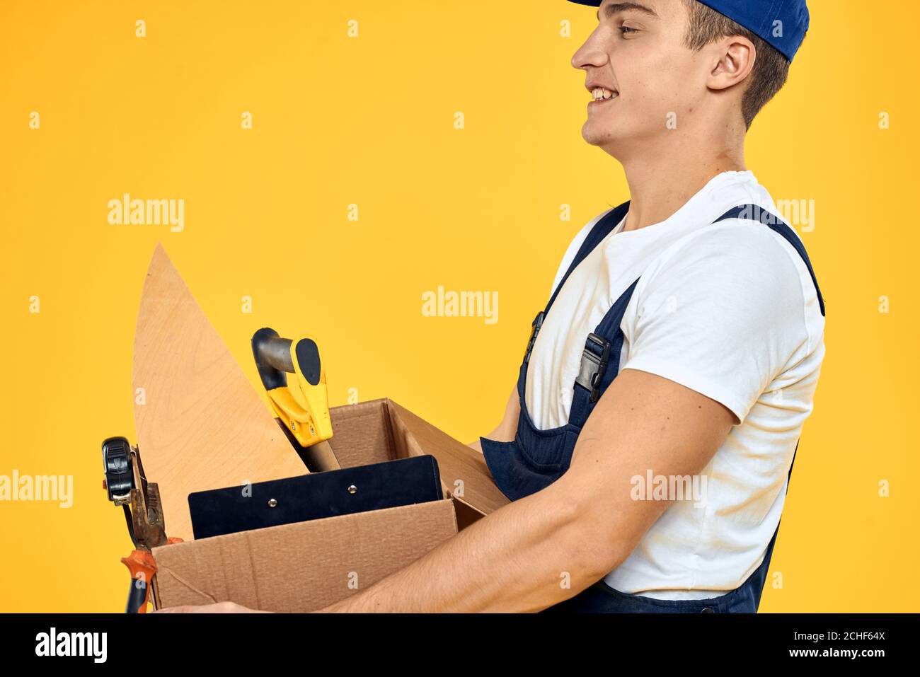 worker with box in hand tools loader yellow background Stock Photo - Alamy