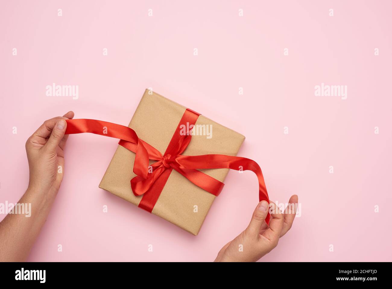 female hands untie a red ribbon on a gift wrapped in brown kraft paper ...