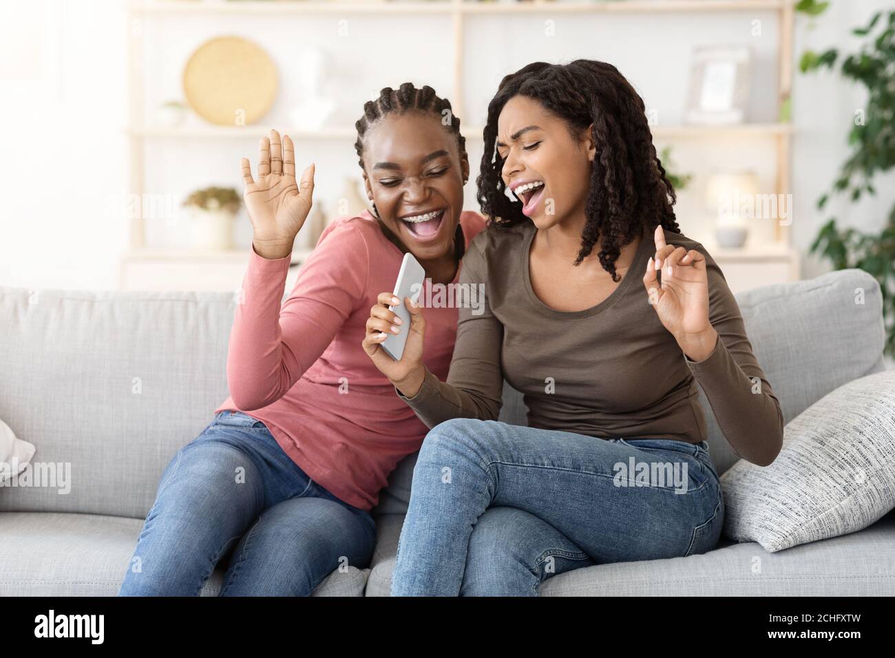Two cheerful young female friends singing at home Stock Photo - Alamy