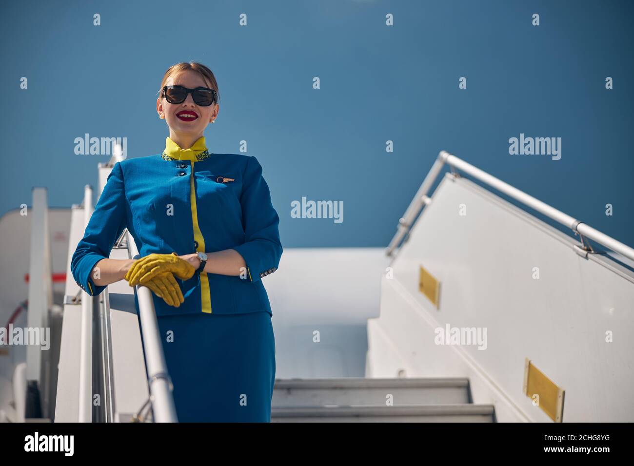Cheerful stewardess standing on airplane steps under blue sky Stock ...