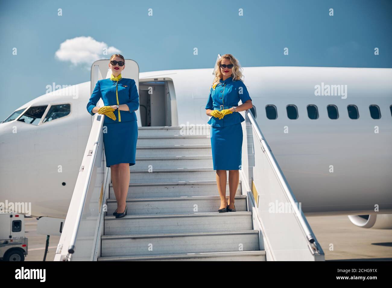 Charming stewardesses standing on airplane stairs under blue sky Stock ...