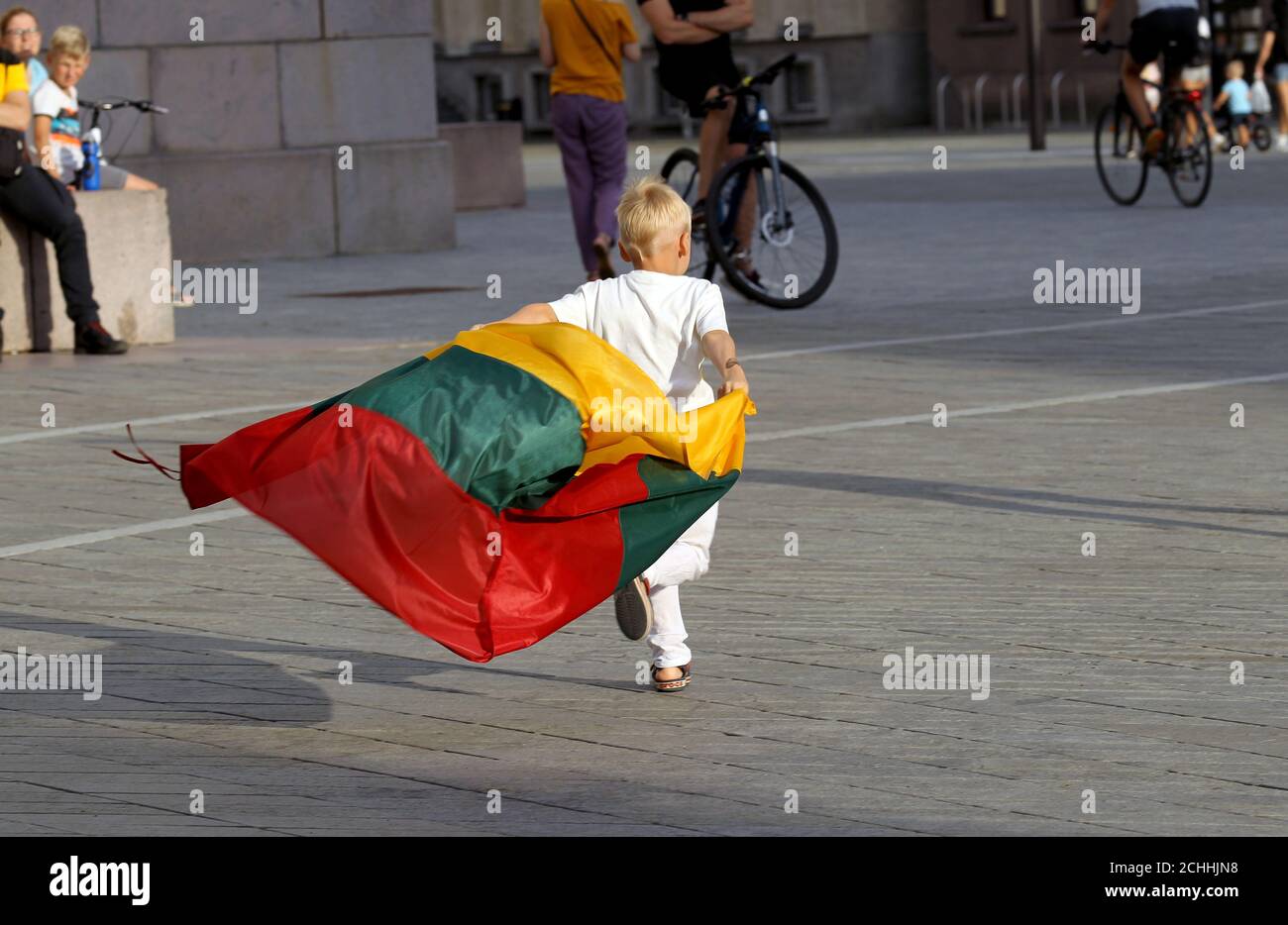 A child carries a fluttering tricolor Lithuanian flag outdoors. Kaunas ...