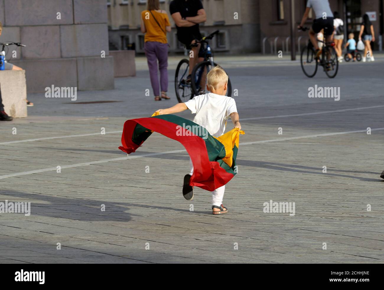A child carries a fluttering tricolor Lithuanian flag outdoors. Kaunas ...