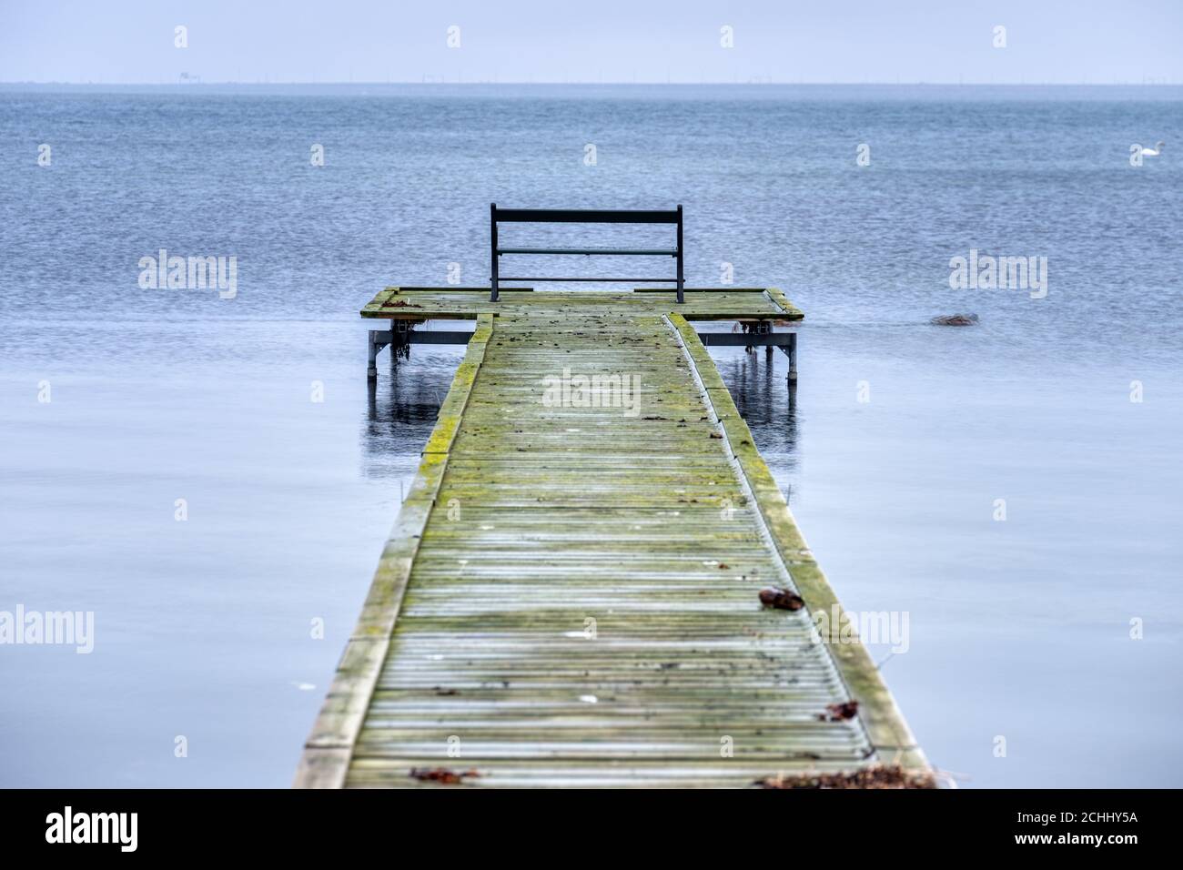Lone bench amid winter gloominess and haziness faces a melancholic sea ...