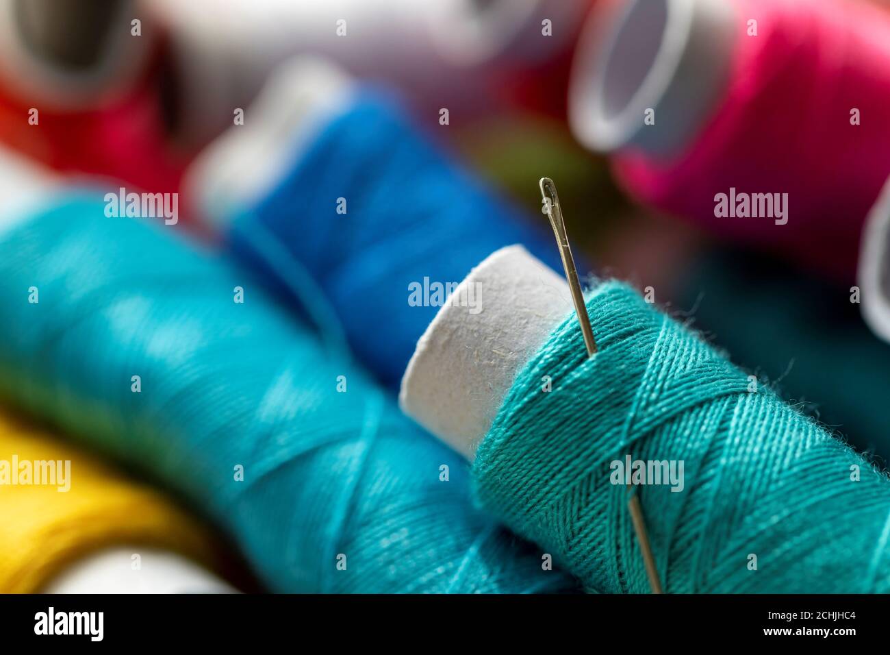 A portrait of a sewing needle put through a roll of thread. The spool ...