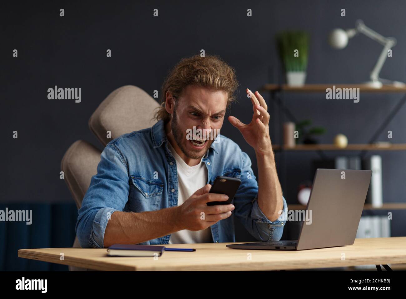 Angry young handsome curly man using laptop. Stressed freelancer lost ...