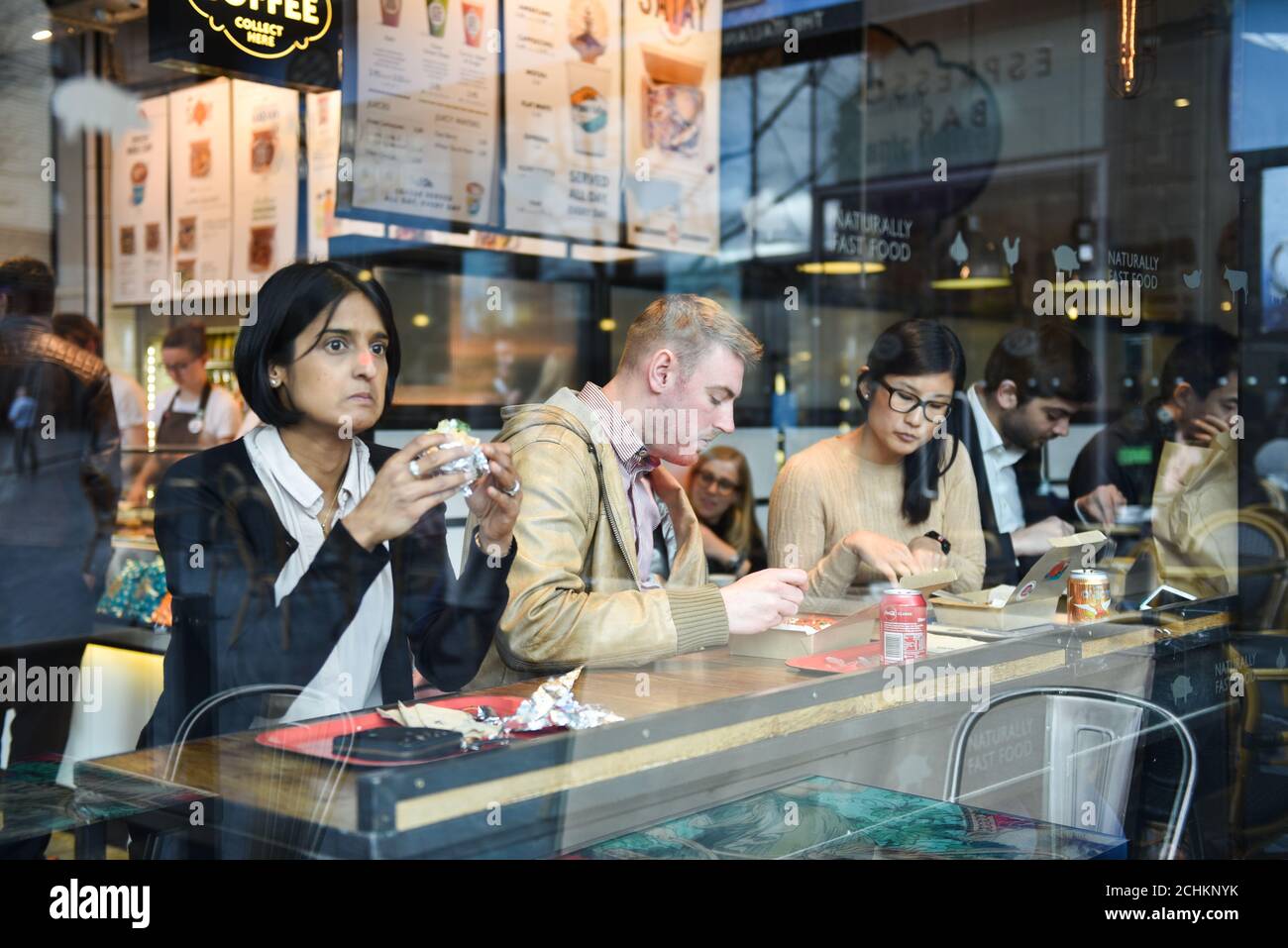 People sit and dine at a fast food cafe, looking behind the window ...