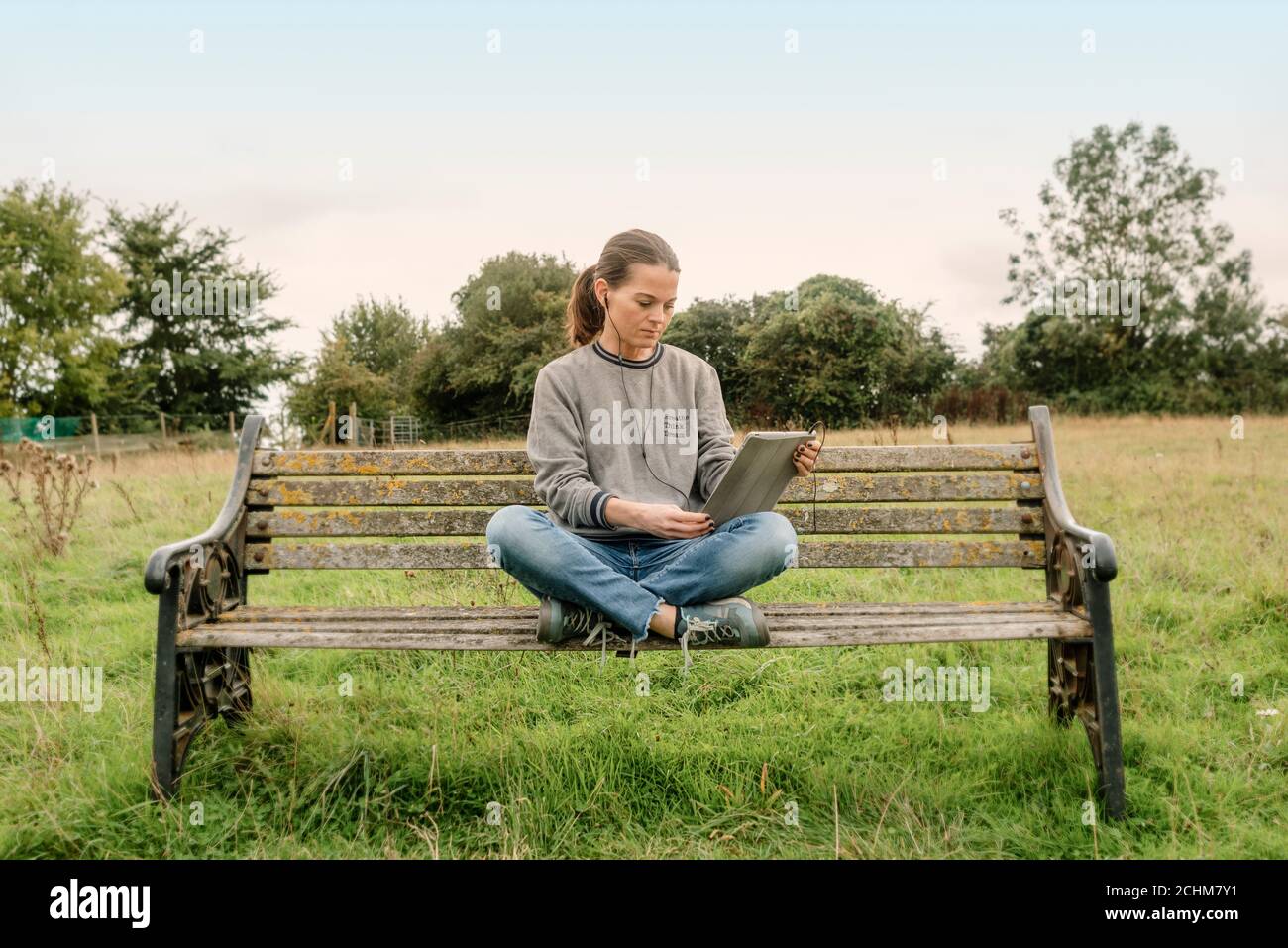 Woman sitting crossed legged on a park bench with a tablet computer ...