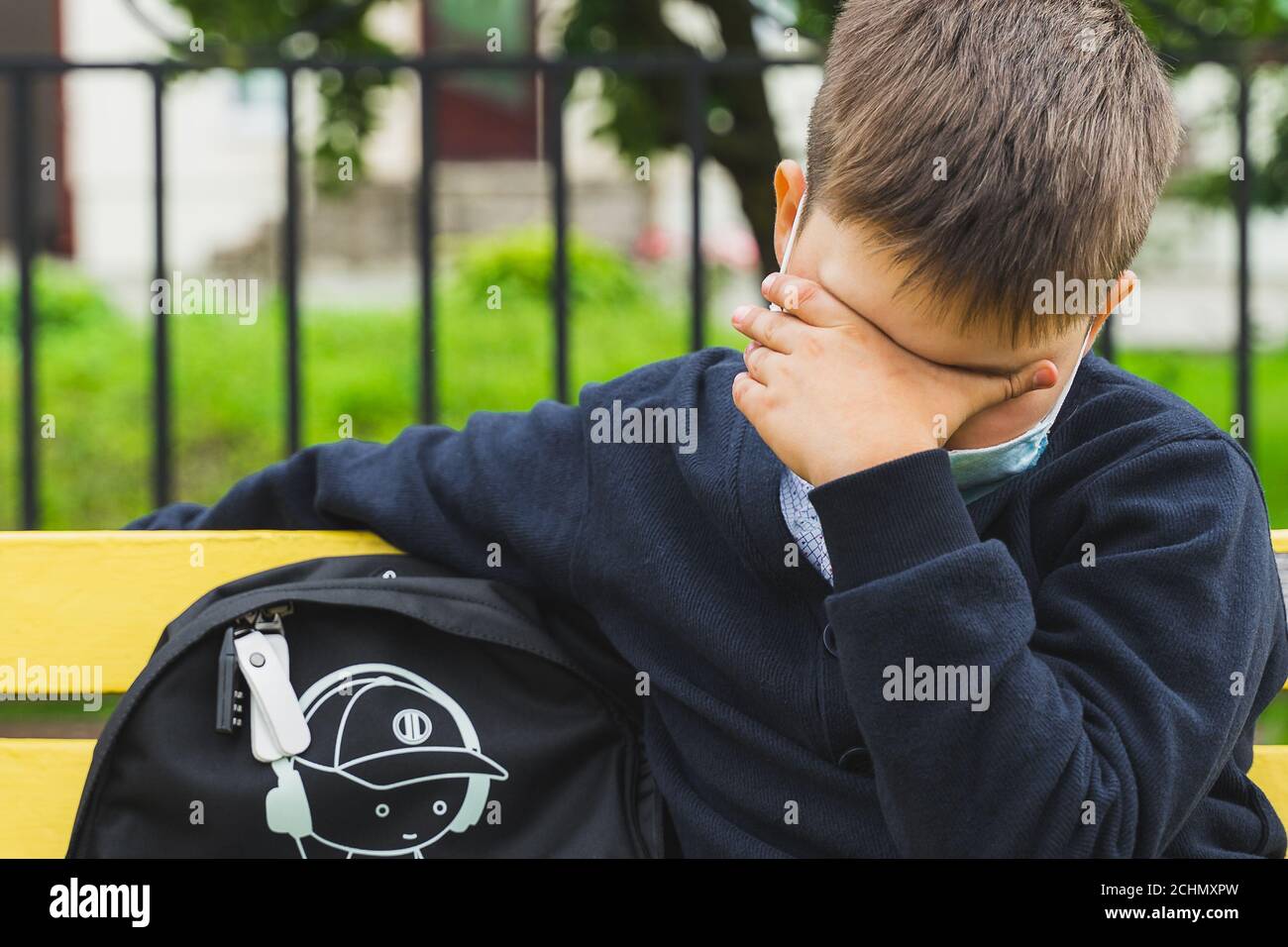 kid closing eyes with hands in mask tired of quarantine. sad school boy ...