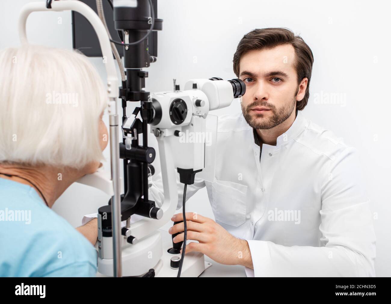 Optometrist doctor using a binocular slit-lamp examines the eye of an ...