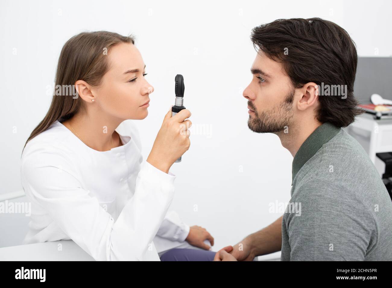 Woman optometrist examining a man's eyes with an ophthalmoscope. Eye ...