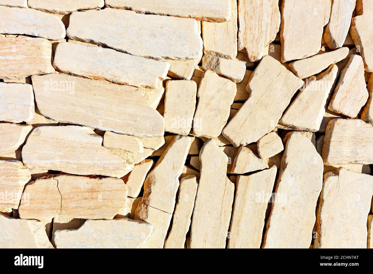 The texture of layered chunks of yellow sandstone in harsh sunlight, separated by stripes of ...