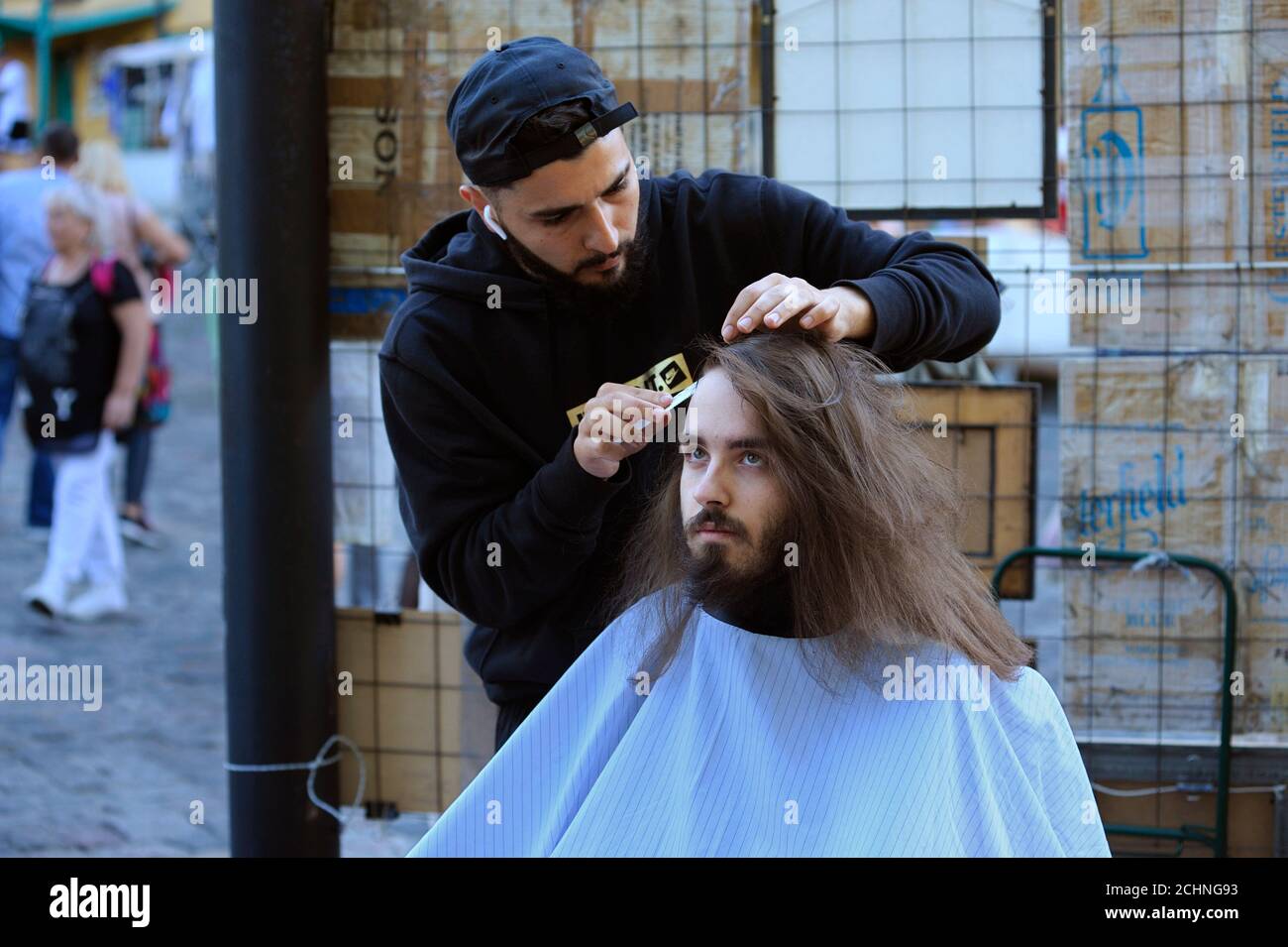 Street barber doing young man's hair on the street, people walking on a ...