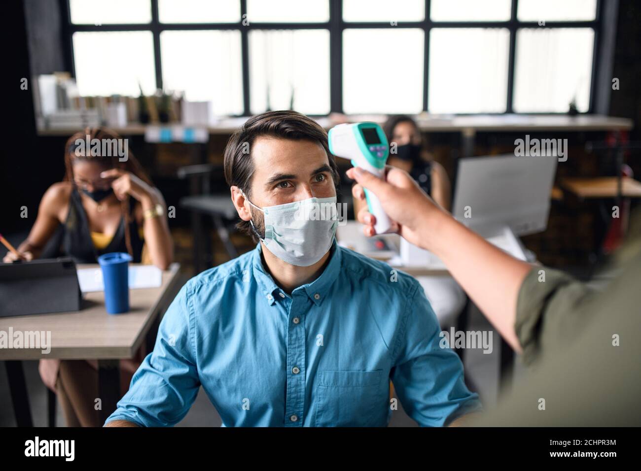 Business people with face masks measuring temperature in office ...