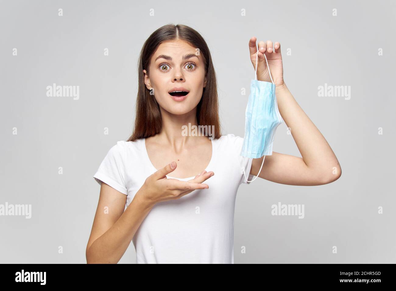 woman Wide open mouth surprised look medical mask in hand white t-shirt ...