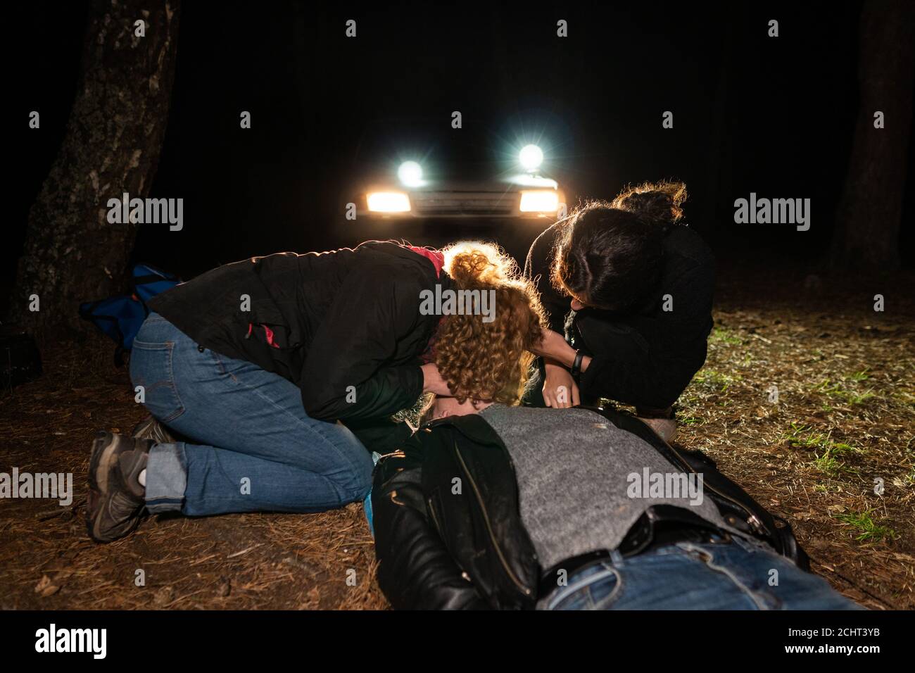 Field First Aid Training. Two women help a man by the headlights of a ...