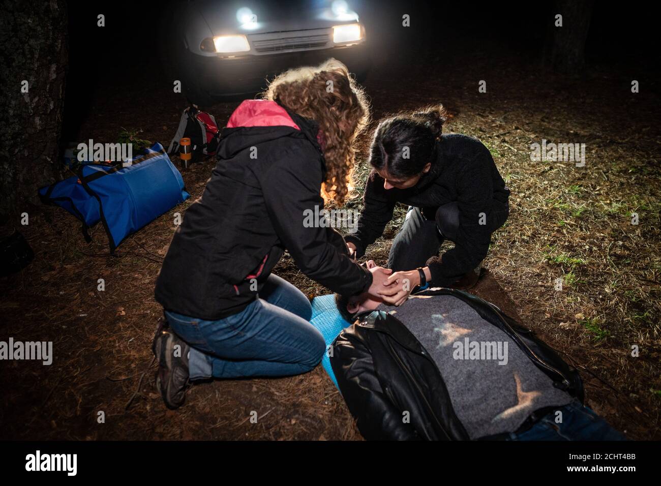 Field First Aid Training. Two women help a man by the headlights of a ...