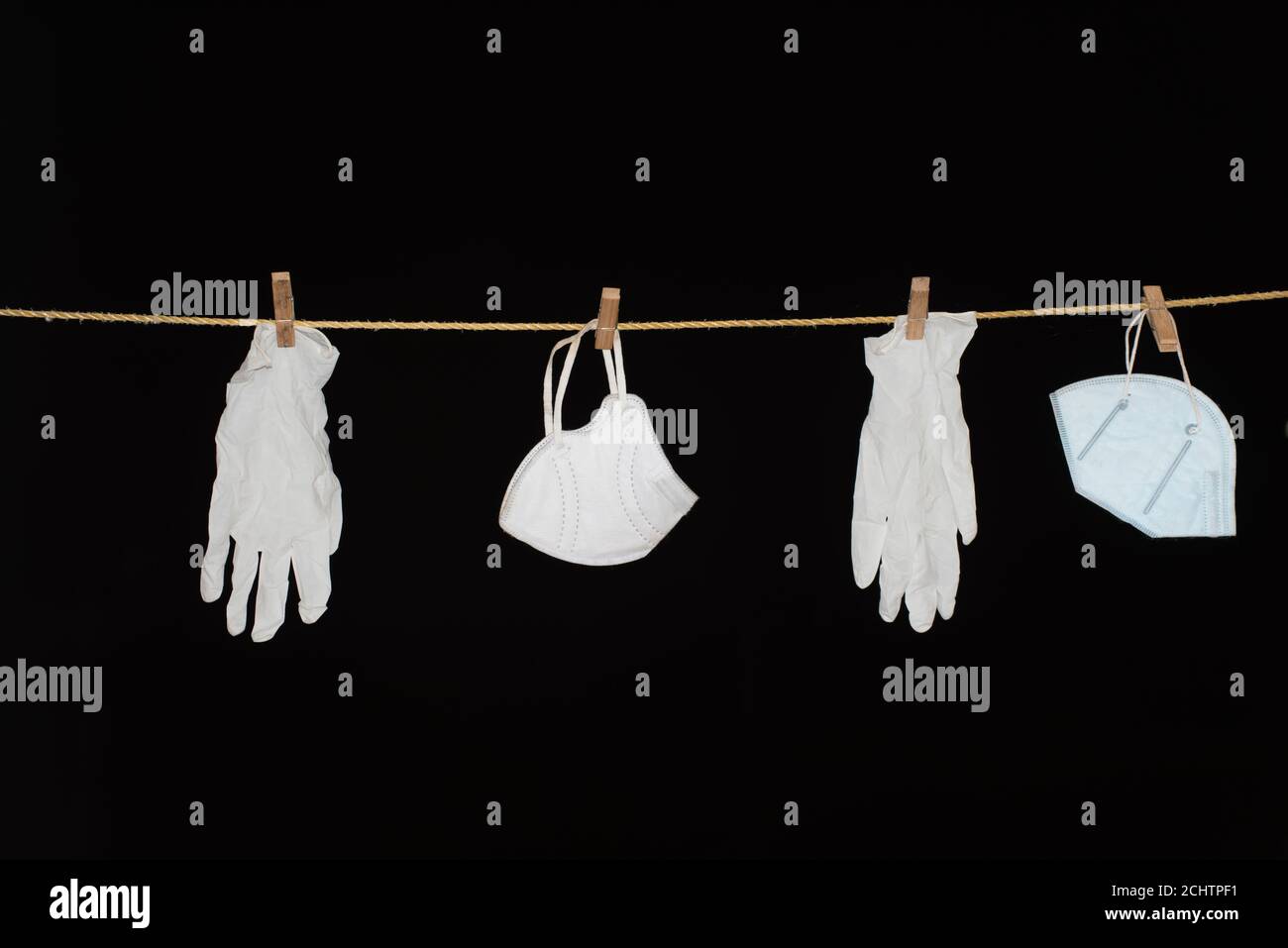 Mask and hand gloves are hanging from rope on isolated black background ...