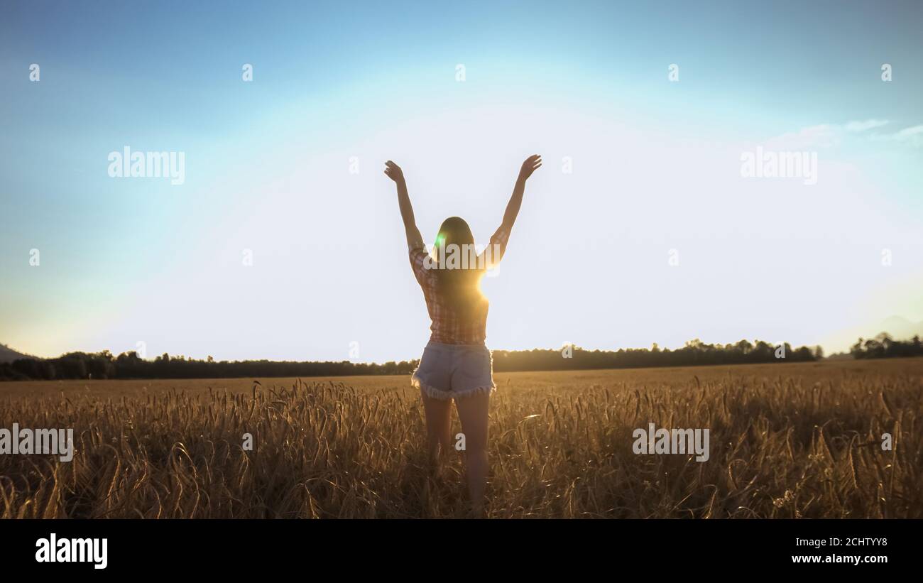 Happy woman walking on a wheat field with open arms at the bright sun ...