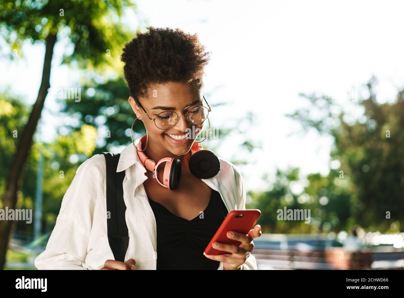 Pretty happy teenager girl texting in a smart phone in a park with a ...